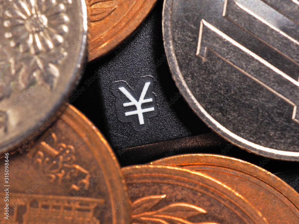 The symbol of the yen. Japanese money coins lie on a black computer or ...