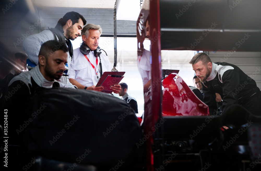 Manager driver talking behind pit crew working on race car in repair ...