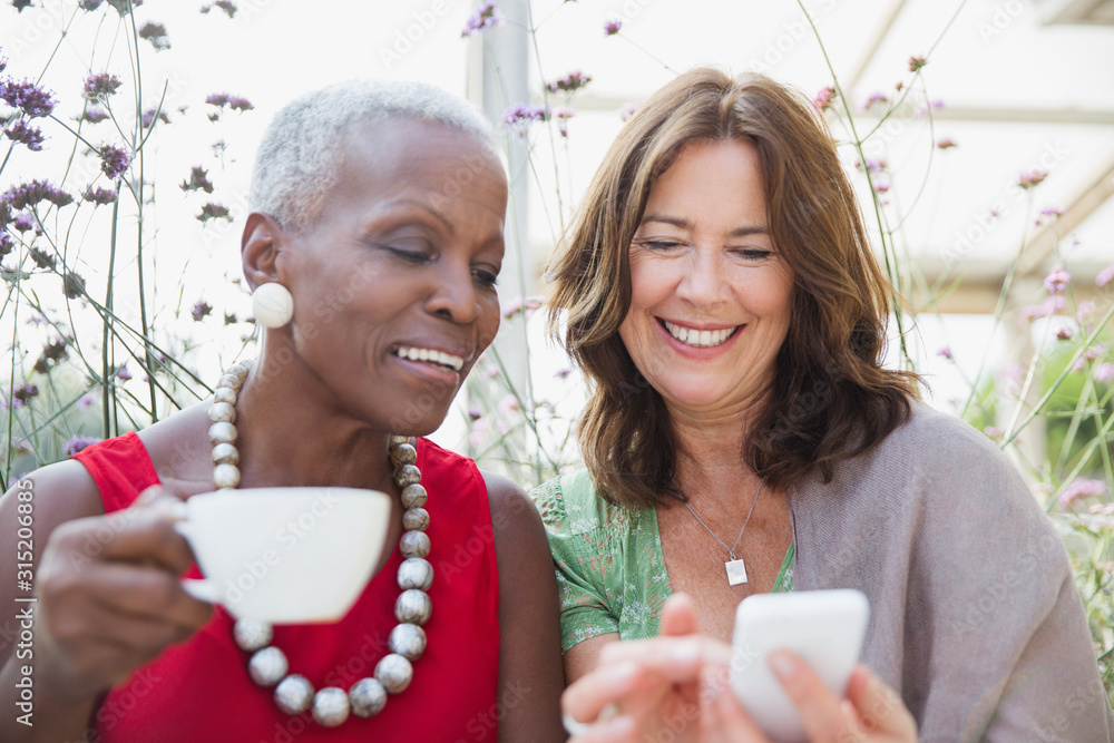 Smiling mature women friends drinking coffee and using cell phone Stock ...