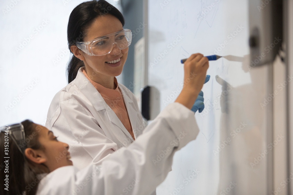 Female science teacher and girl student writing at whiteboard in ...