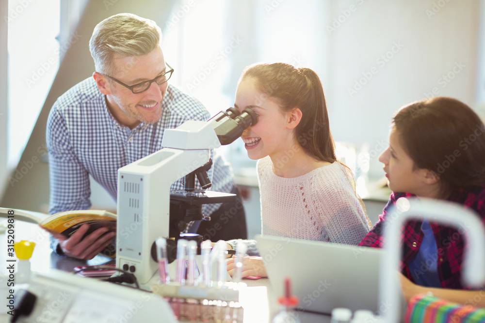 Male teacher helping girl student using microscope, conducting ...