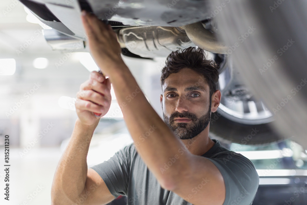 Portrait serious male mechanic working under car in auto repair shop ...