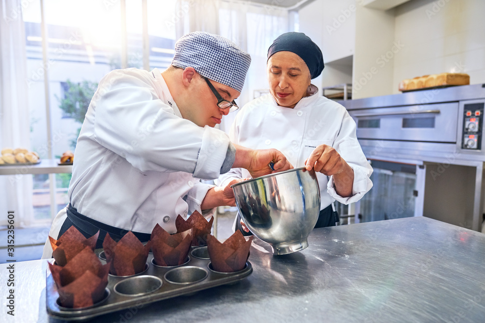 Chef helping student with Down Syndrome baking muffins in kitchen Stock ...