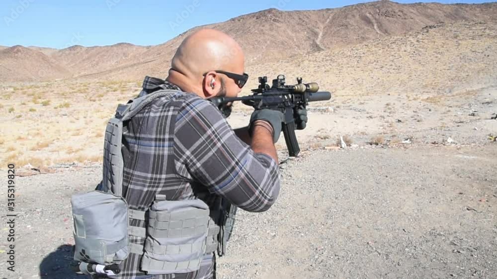 Bald man with a beard firing an assault rifle at an outdoor shooting ...