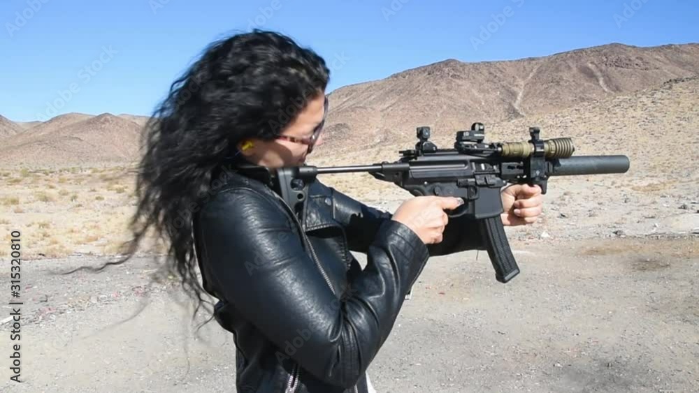 Brunette woman firing a rifle at a metal target at a desert shooting ...