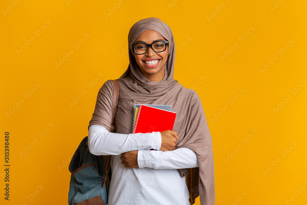 Happy black muslim student girl in hijab with backpack and notepads ...
