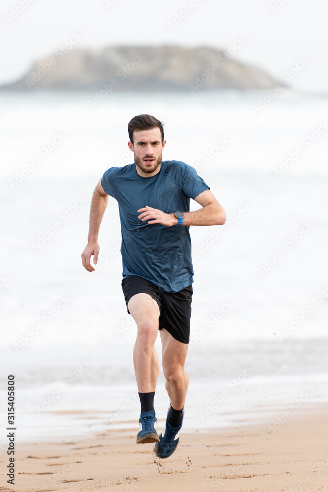 Bearded male athlete in active wear running during empty sandy beach ...