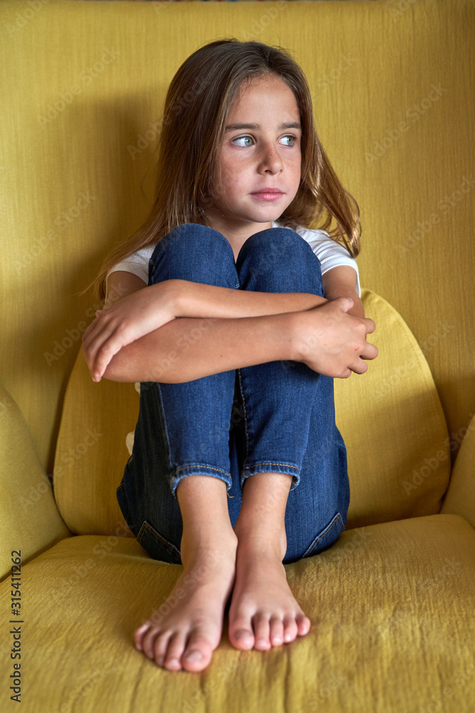 Wistful little girl in white t shirt and jeans sitting with tighten ...