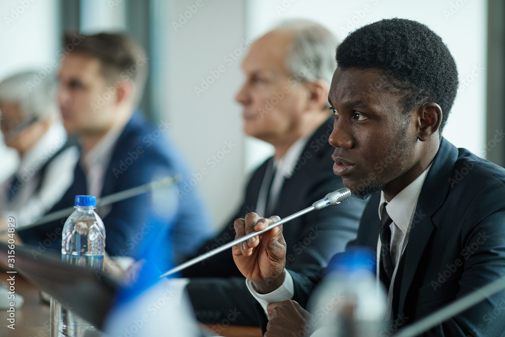 Serious African businessman in black suit sitting and speaking the ...