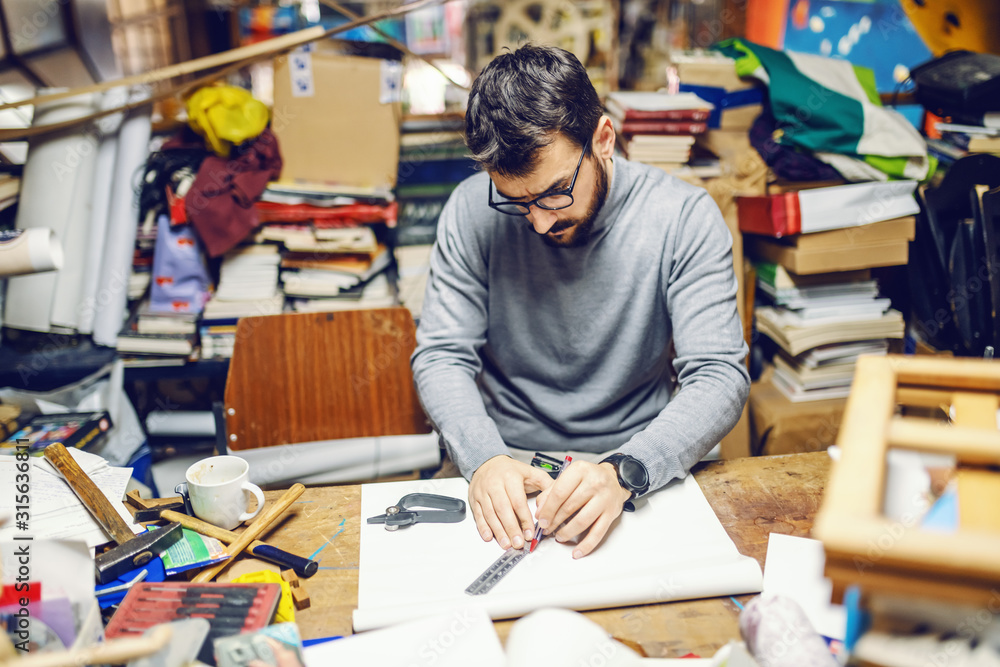 Young focused handsome Caucasian bearded bookbinder sitting in back of ...
