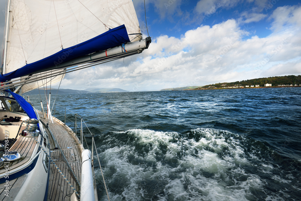 Sloop rigged modern yacht with wooden teak deck sailing on a cloudy day ...