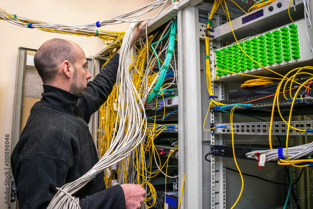 A man untangles many utp wires in racks with computer equipment ...