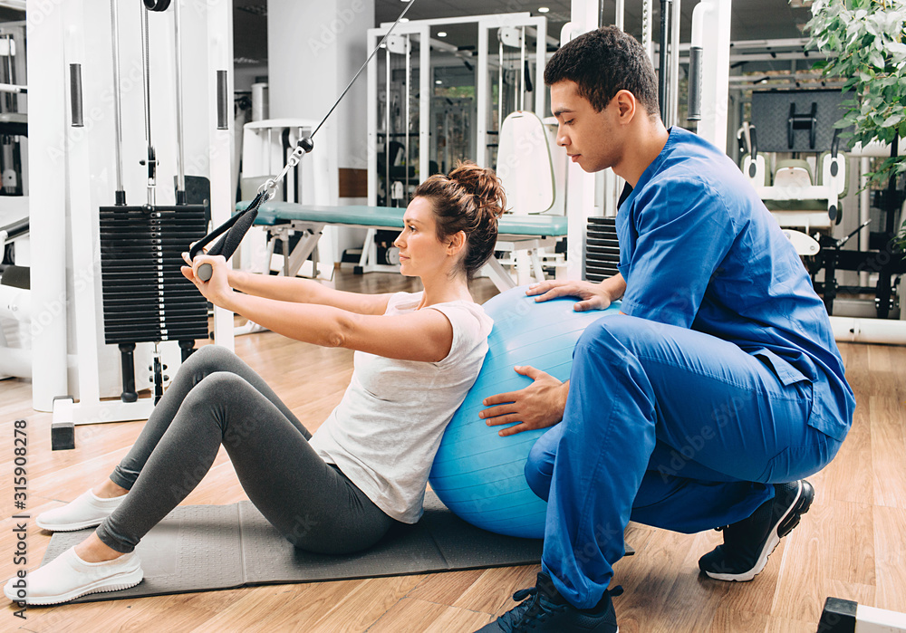 kinesiologist helps a woman do exercises to strengthen her back muscles ...