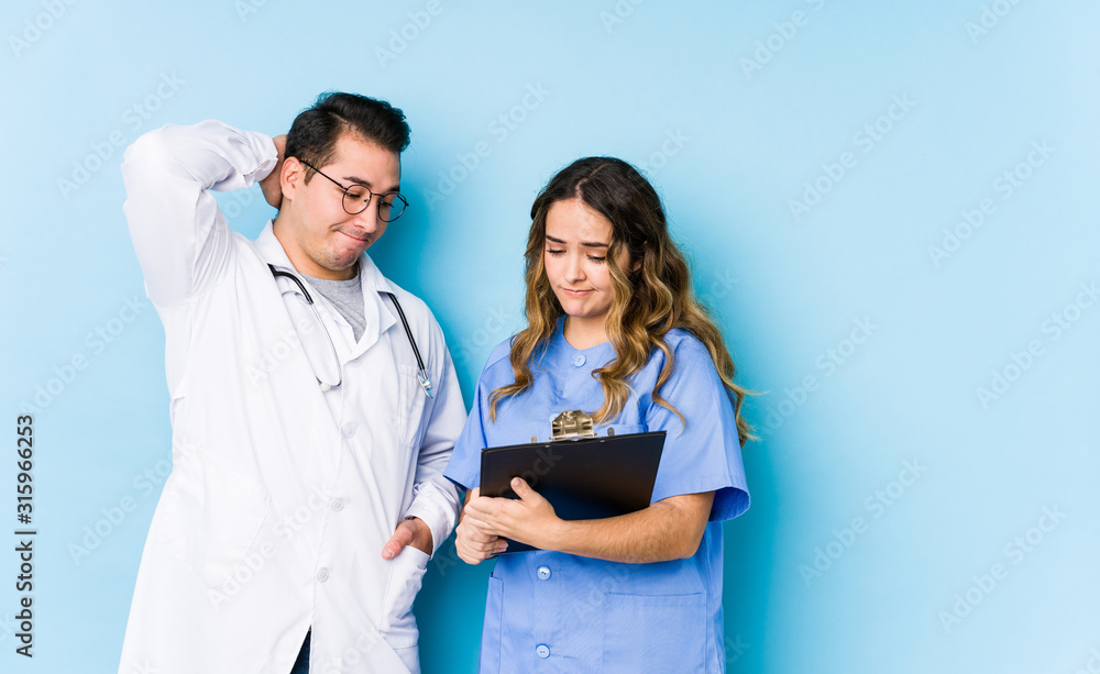 Young doctor couple posing in a blue background isolated touching back ...