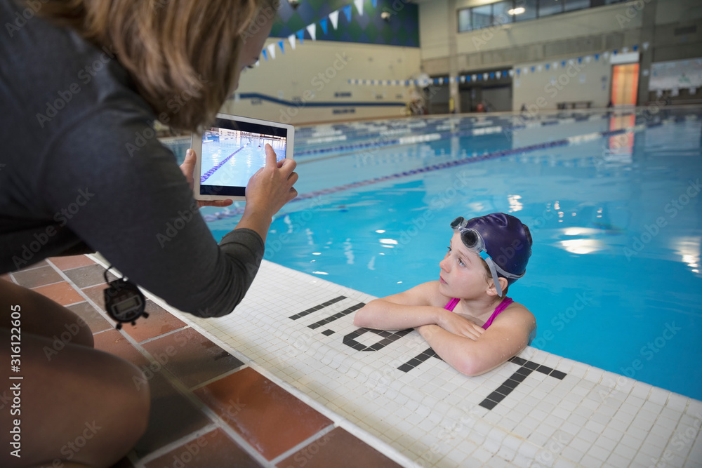 Female coach with digital tablet coaching girl swimmer in swimming pool ...