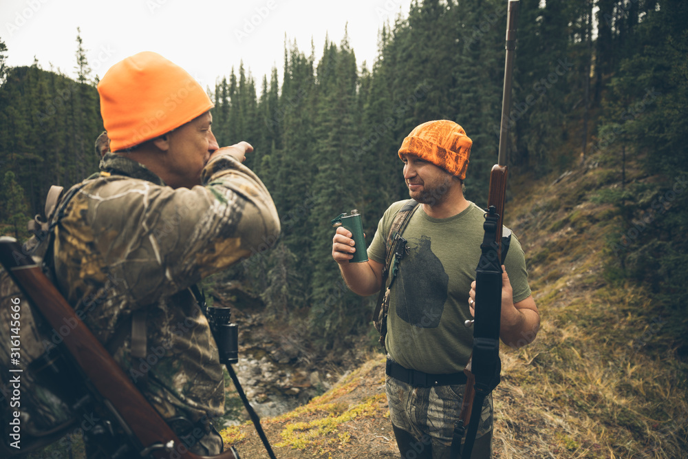 Father and son hunters with hunting rifles drinking alcohol from flask ...