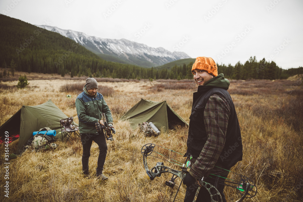 Male hunter friends with hunting compound bow outside tents at campsite ...