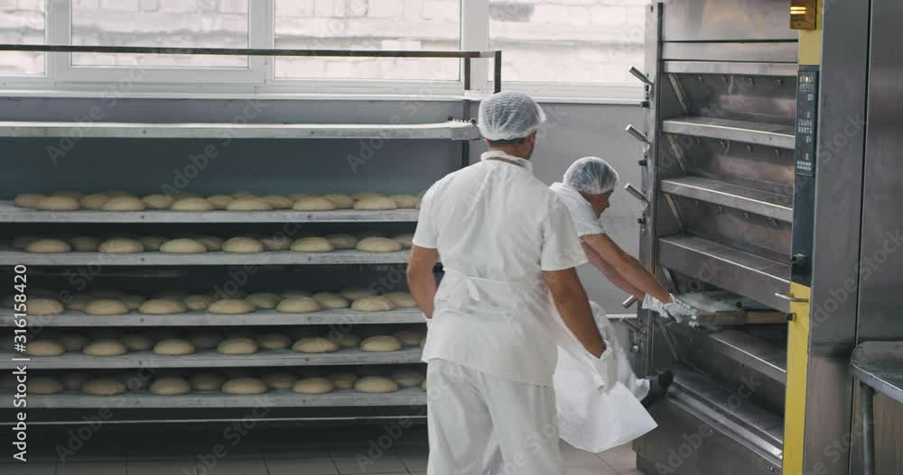 Process of load the raw bread in the oven machine of two bakery workers ...