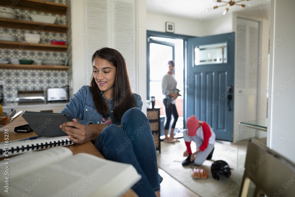Smiling tween girl doing homework, using digital tablet while mother ...