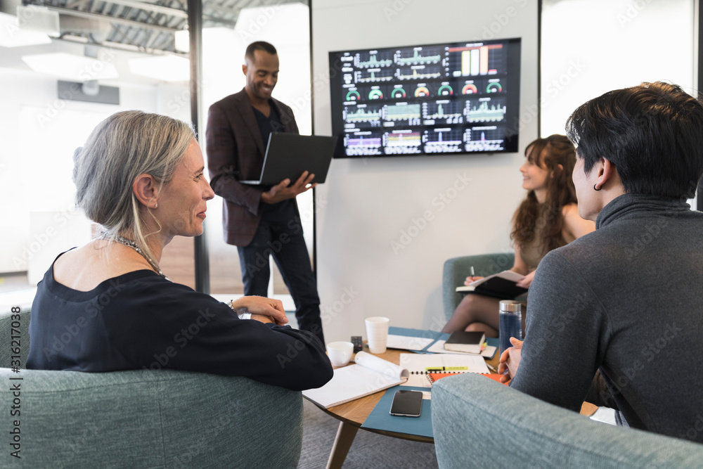 Man using laptop presenting to colleagues with monitor on wall foto de ...
