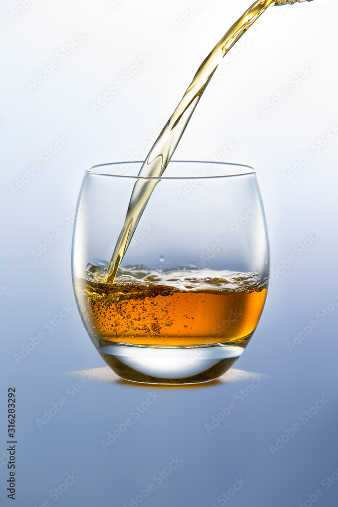 Whiskey pouring from the neck of a bottle into a glass on a wooden ...