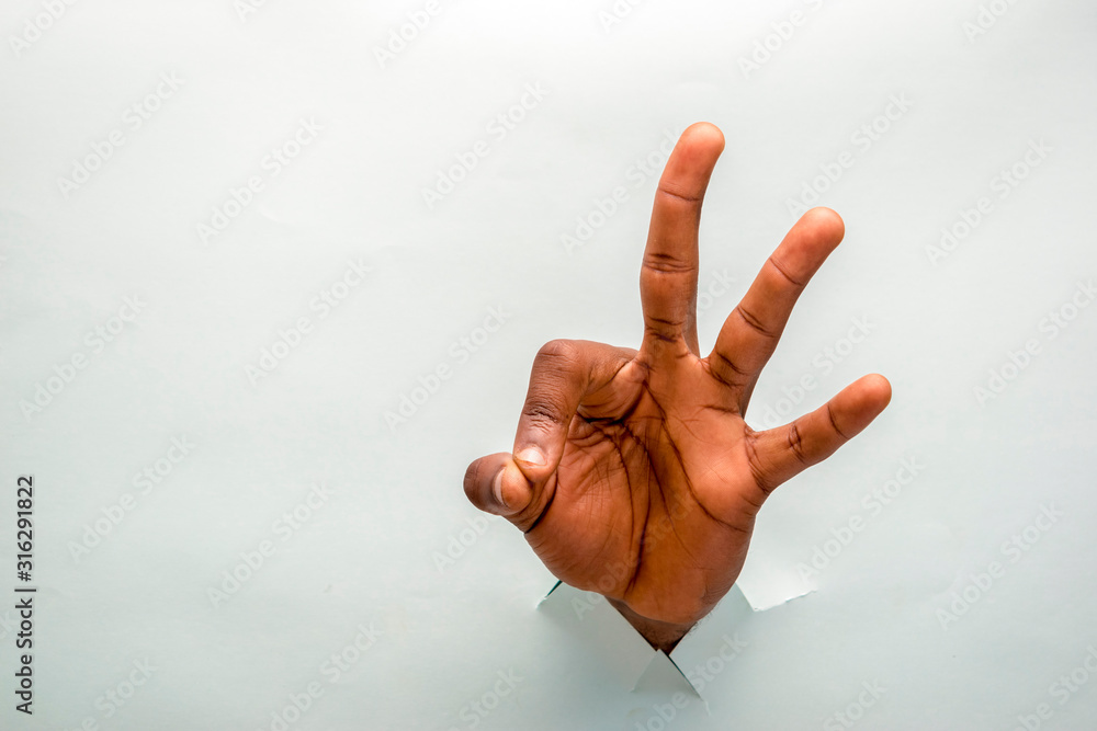 black person hand through a hole in a cardboard making ok sign, showing ...