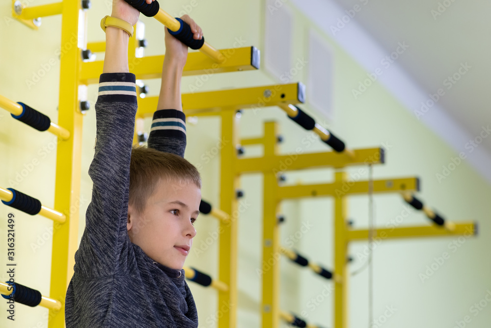 Young child boy exercising on a wall ladder bar inside sports gym room ...