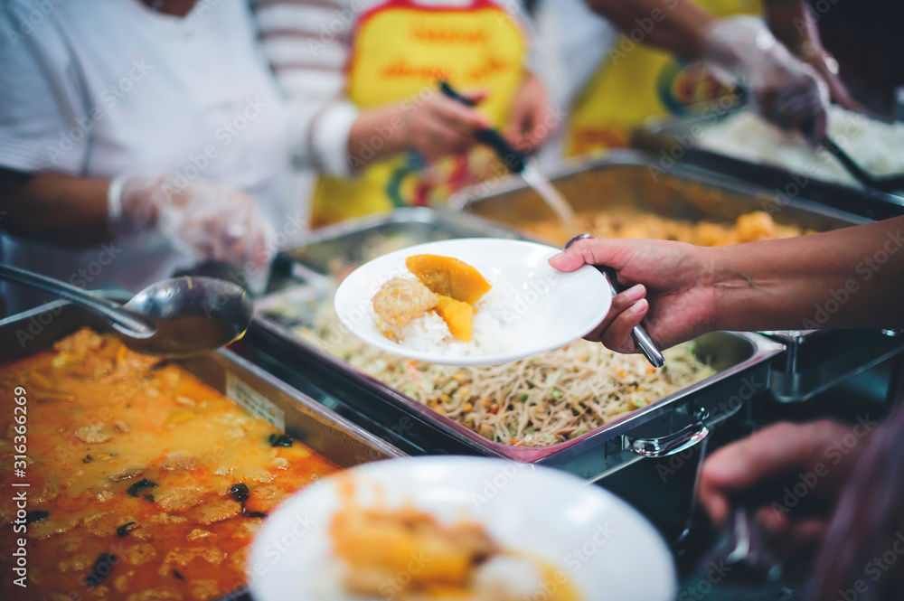The hands of the poor handed a plate to receive food from volunteers to ...