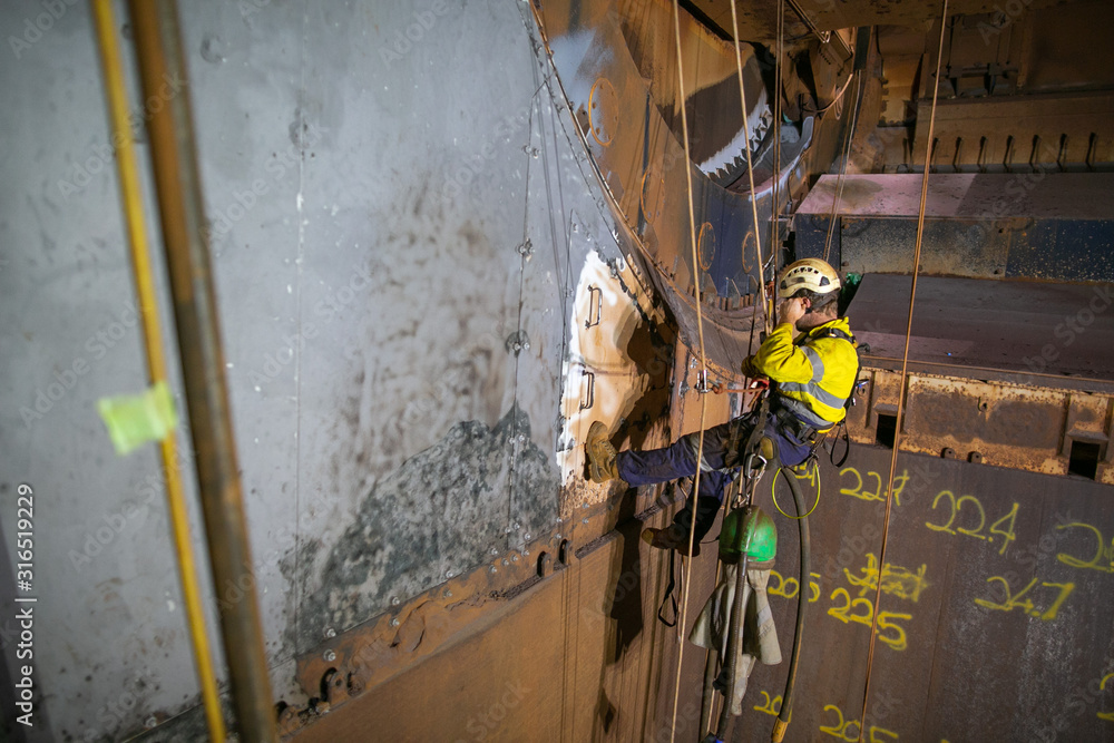 Rope access sandblaster technician wearing fall body safety equipment ...