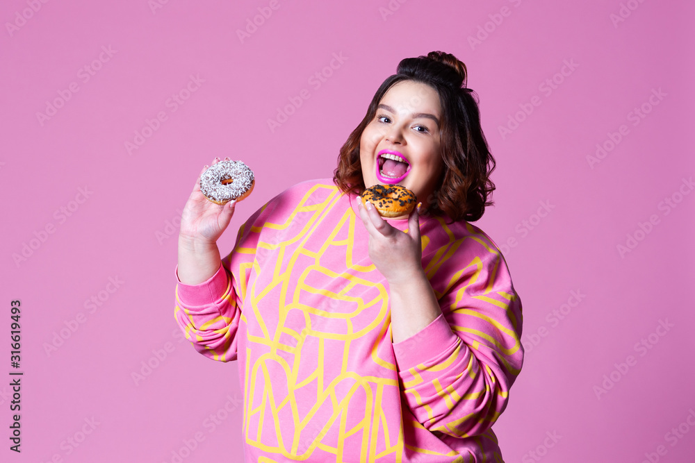 Cheerful plus size model eating doughnuts, fat woman overeats on pink ...
