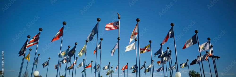 There are 50 State Flags waving in the wind on flagpoles equal distant ...