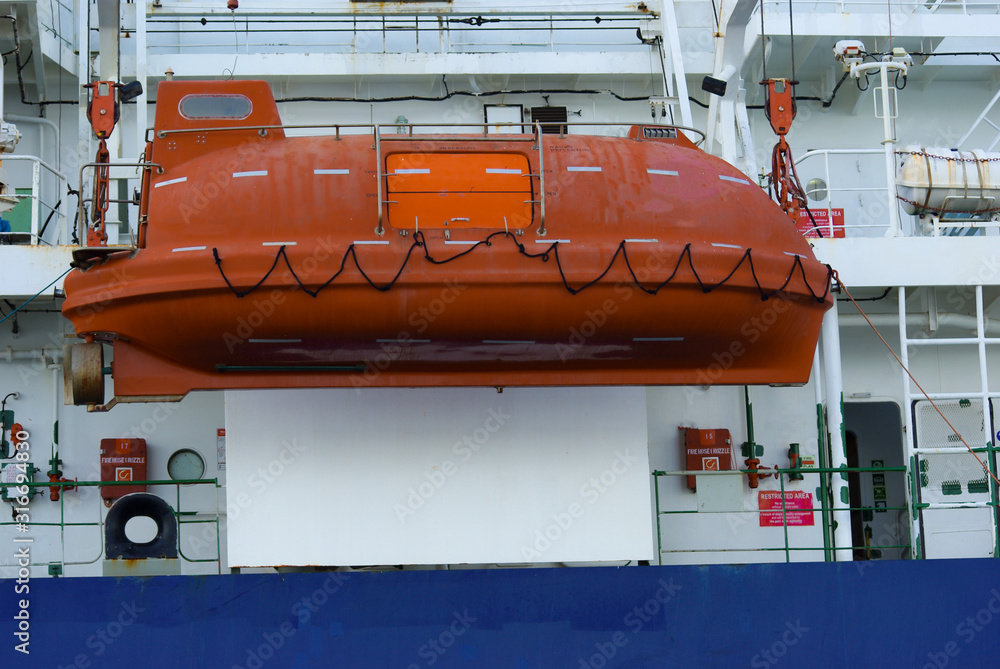 Enclosed safety orange life boat launching on the cargo ship during ...