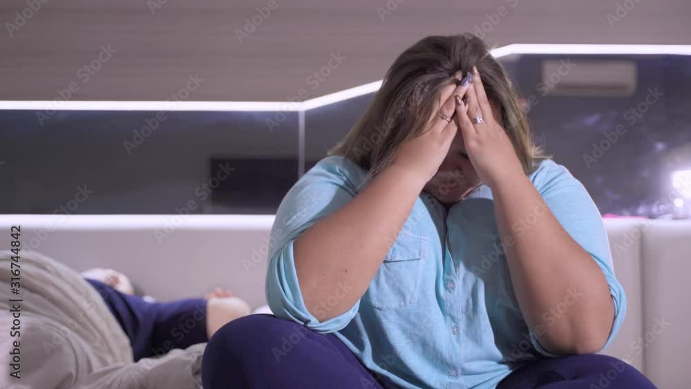 Stressful overweight woman with her husband sleeping on the bed at home ...