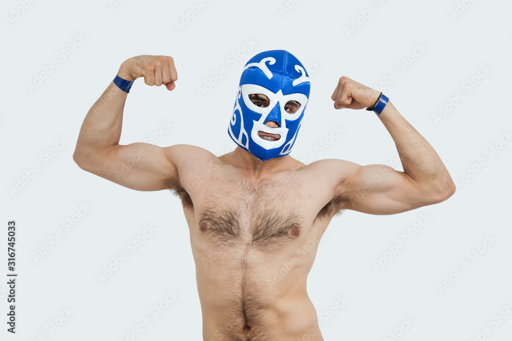 Portrait of a shirtless man in wrestling mask flexing muscles over gray ...