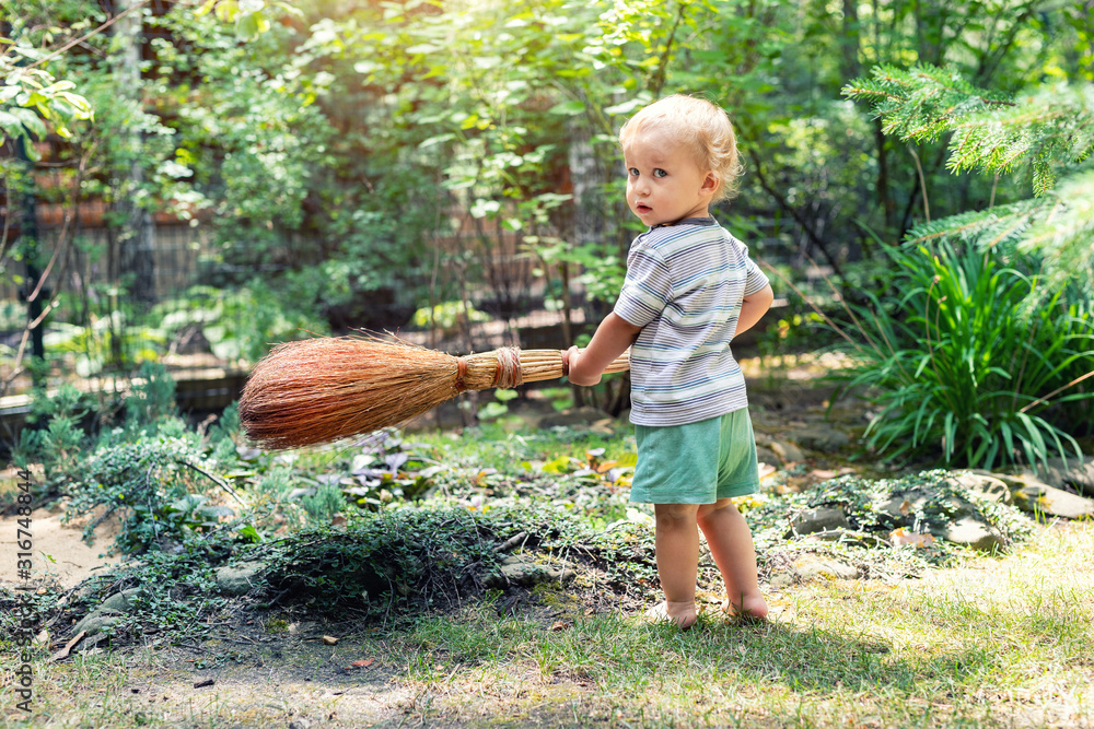 Cute adorable caucasian toddler boy playing holding broom at backyard ...