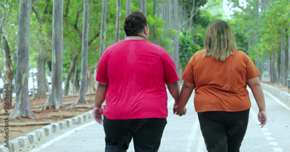 Back view of obese couple walking at the park while holding hands. Shot ...