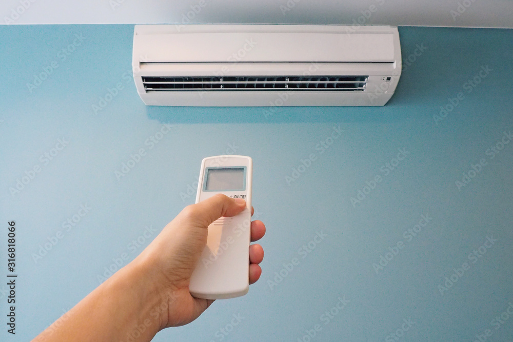 Man Pressing Button On Air Conditioner Remote Control After Using To Save Power And Cost man-pressing-button-on-air-conditioner-remote-control-after-using-to-save-power-and-cost