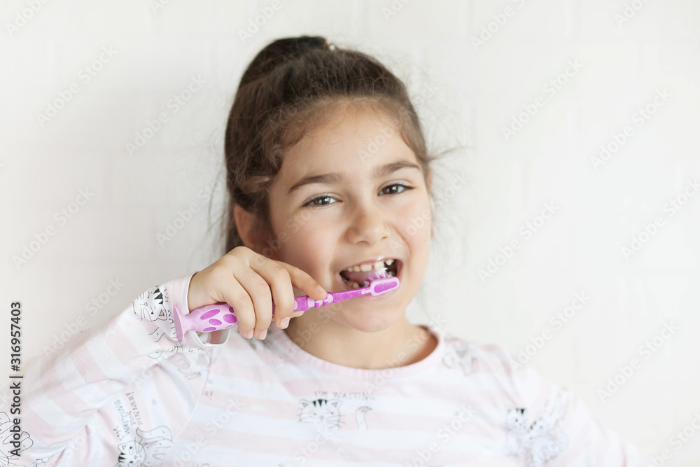Happy cute little child girl brushing her teeth on light background ...