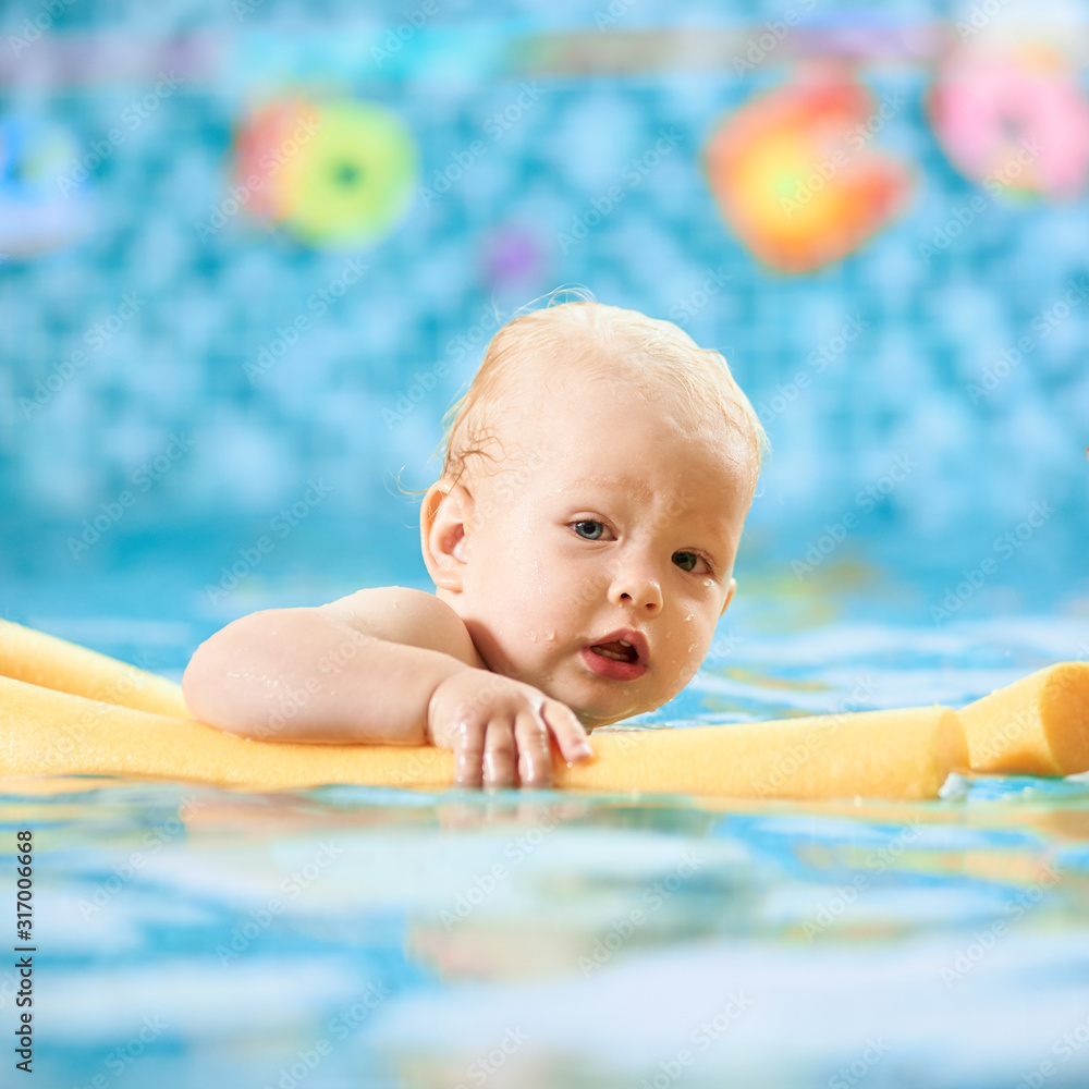 Portrait of cute little boy holding a pool-noodle and trying to swim ...
