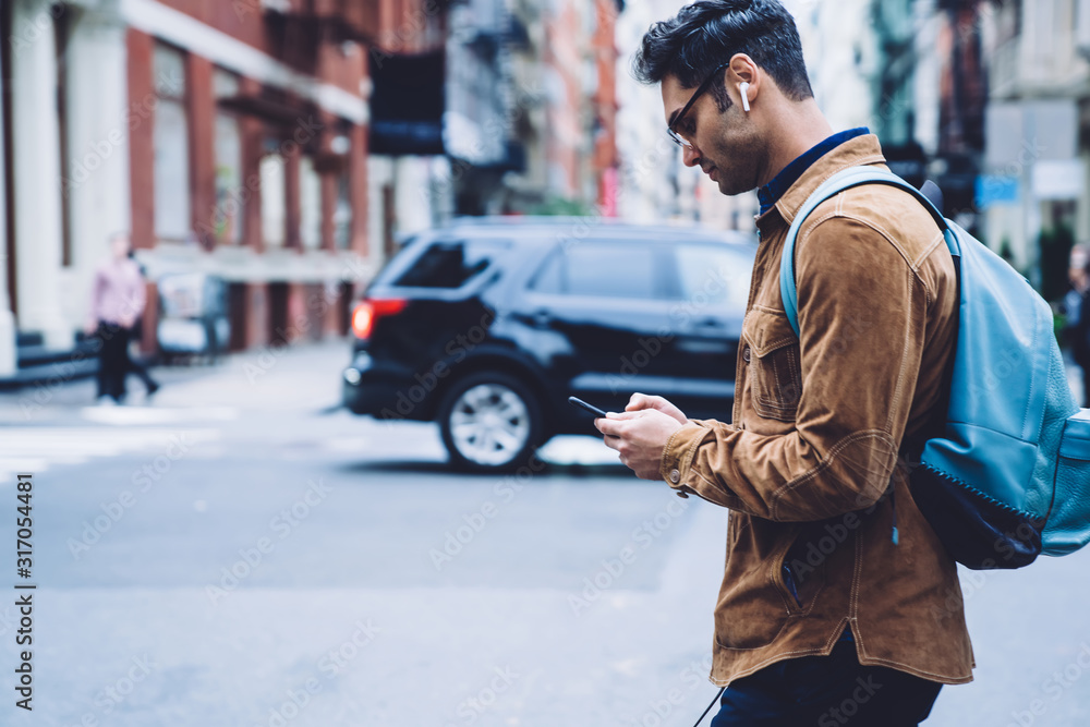 Thoughtful Hispanic man walking down street and texting on smartphone ...