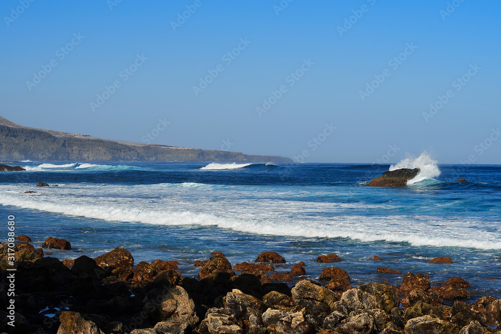 Costa con rocas en primer plano y mar tranquilo con olas y una ola ...