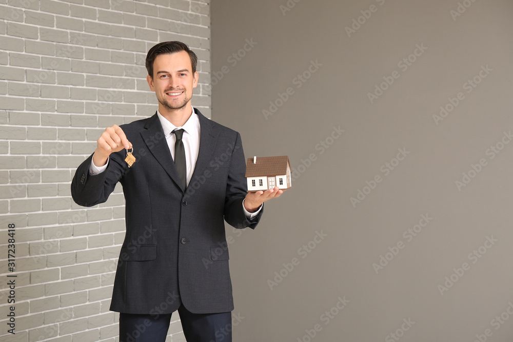 Portrait of male real estate agent with key and model of house indoors ...