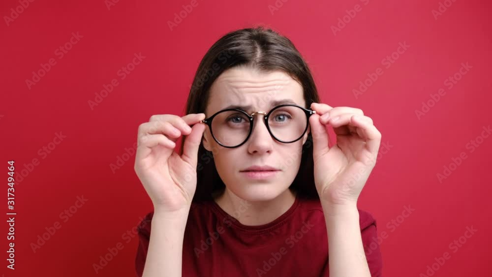 Shocked emotional brunette woman keeps hands on rim of spectacles ...