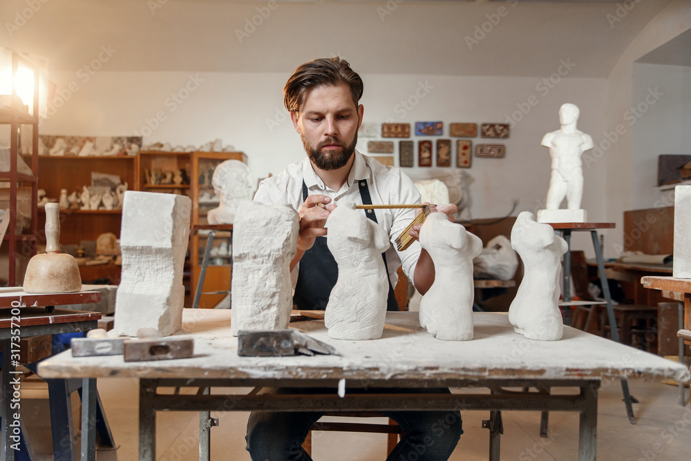 Male craftsman in working uniform makes a limestone copy of woman torso ...