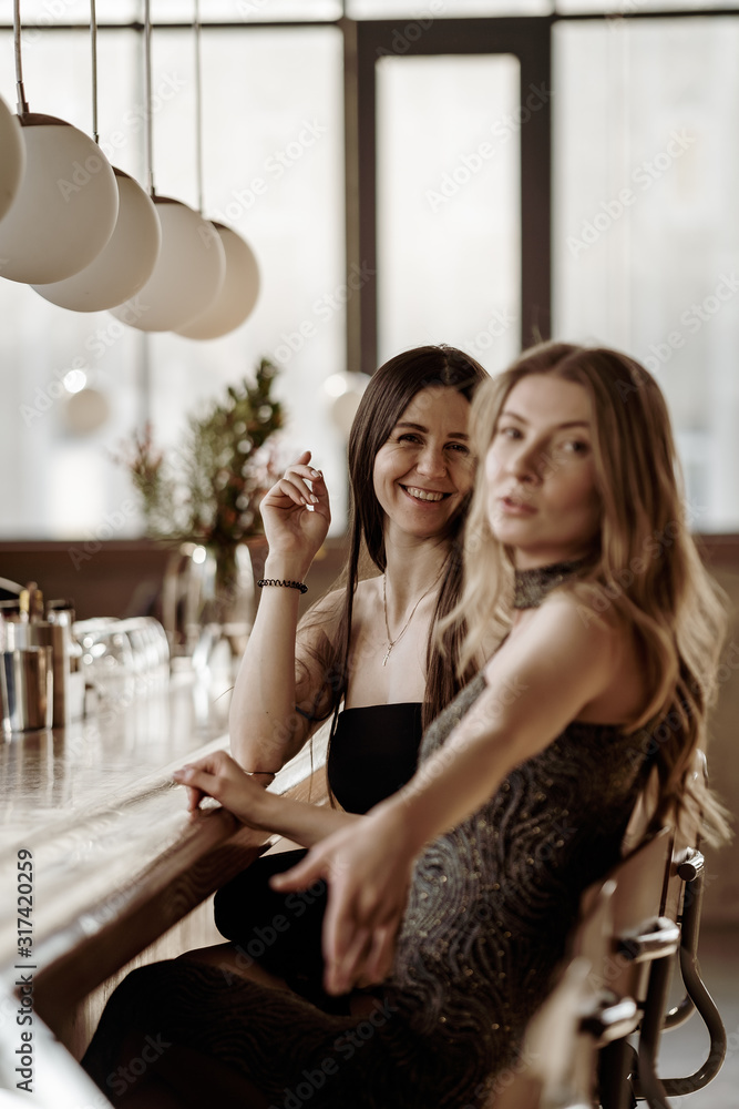 Two gorgeous young women sitting at the bar, day time. Blond and dark ...