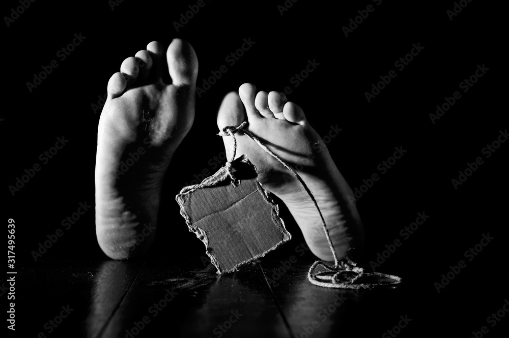 Death concept. Feet of a corpse on a wooden floor wearing a cardboard ...