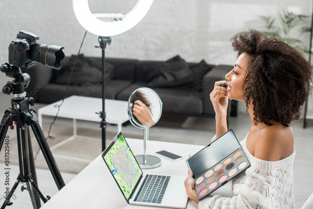 side view of happy african american influencer holding eye shadow ...