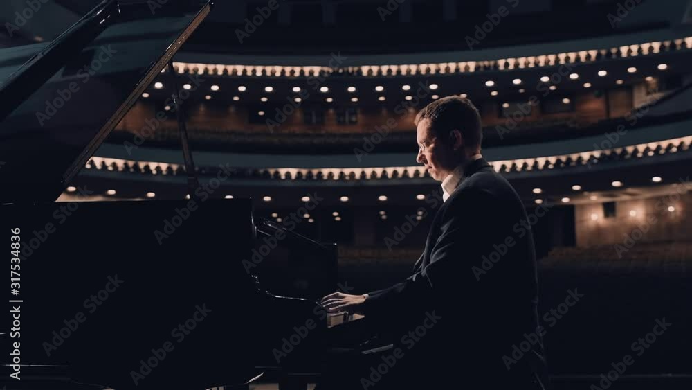 Handsome middle-aged pianist playing on a grand piano on big stage in ...