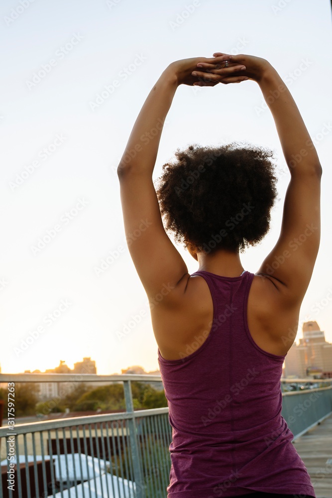Woman in fitness attire stretching arms overhead on pedestrian bridge ...