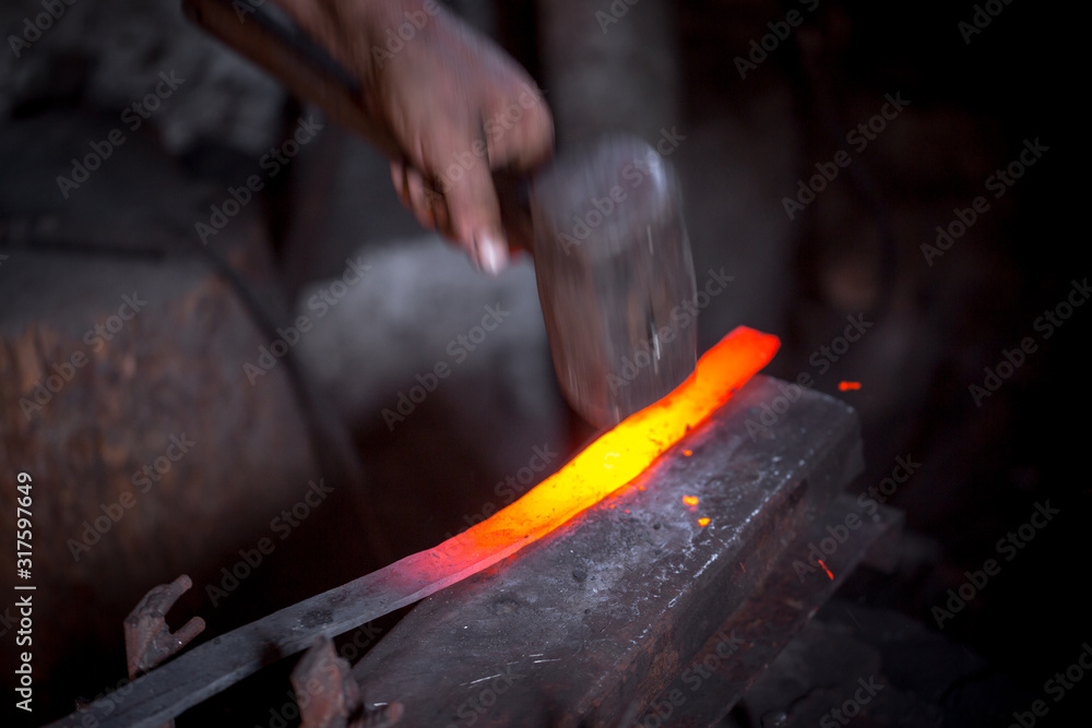 Blacksmith's hands at work. In one hand a hammer, in the other a ...